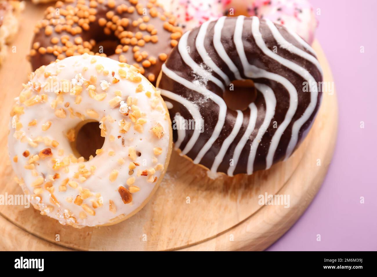 Wooden board with delicious donuts on lilac background, closeup Stock ...