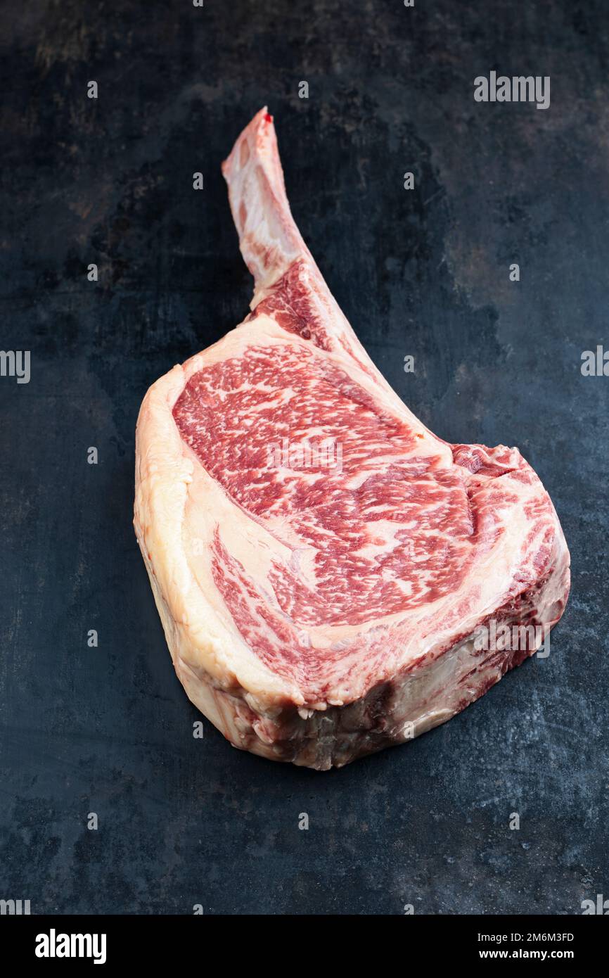 Raw dry aged Wagyu tomahawk steak offered as close-up on an old rustic ...