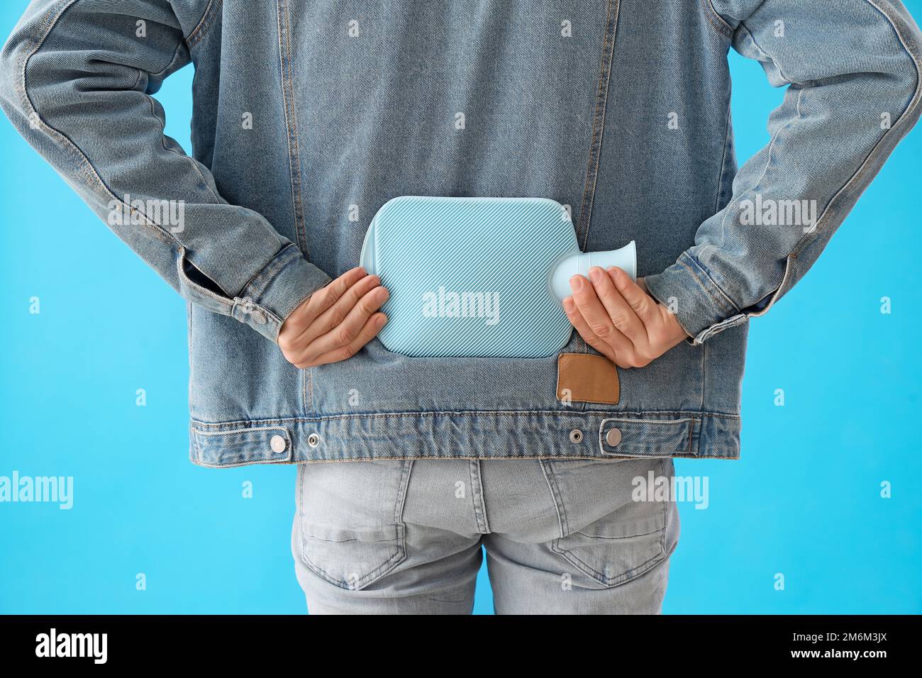 Young man warming his lower back with hot water bottle on blue ...