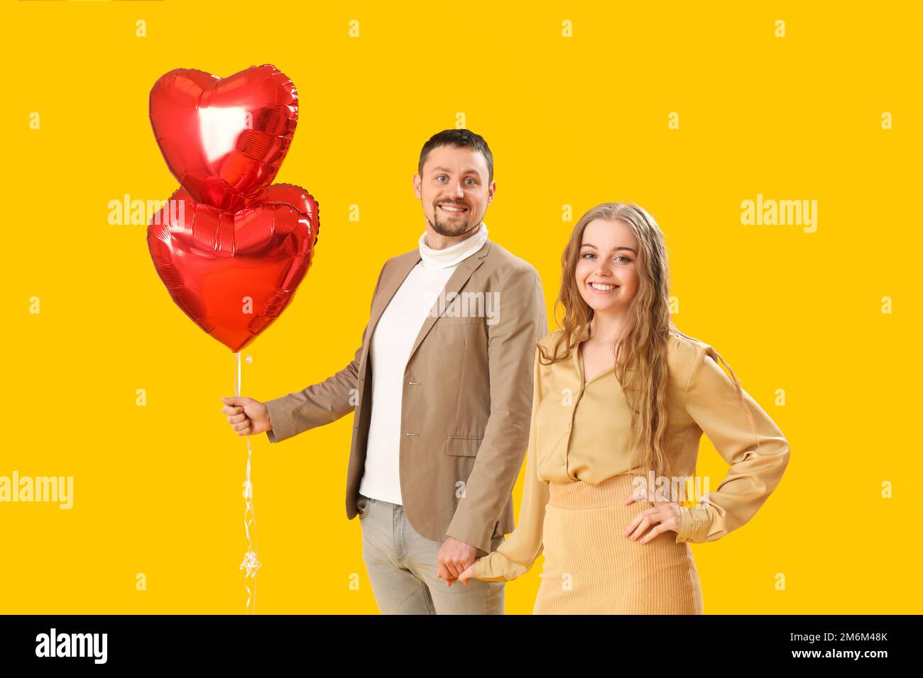 Happy young couple with heart-shaped balloons on yellow background ...
