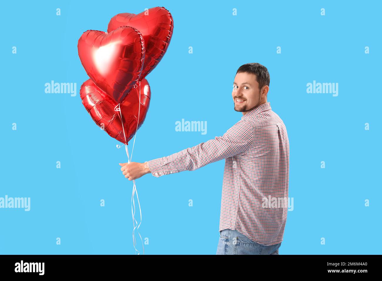 Handsome man with heart-shaped balloons on light blue background ...