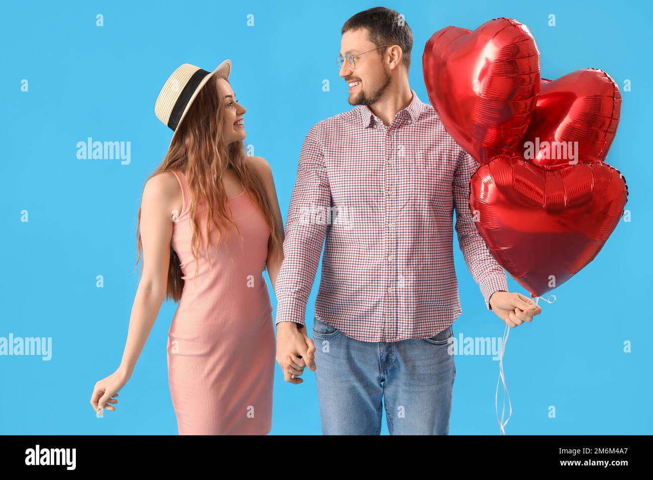 Happy young couple with heart-shaped balloons on blue background ...