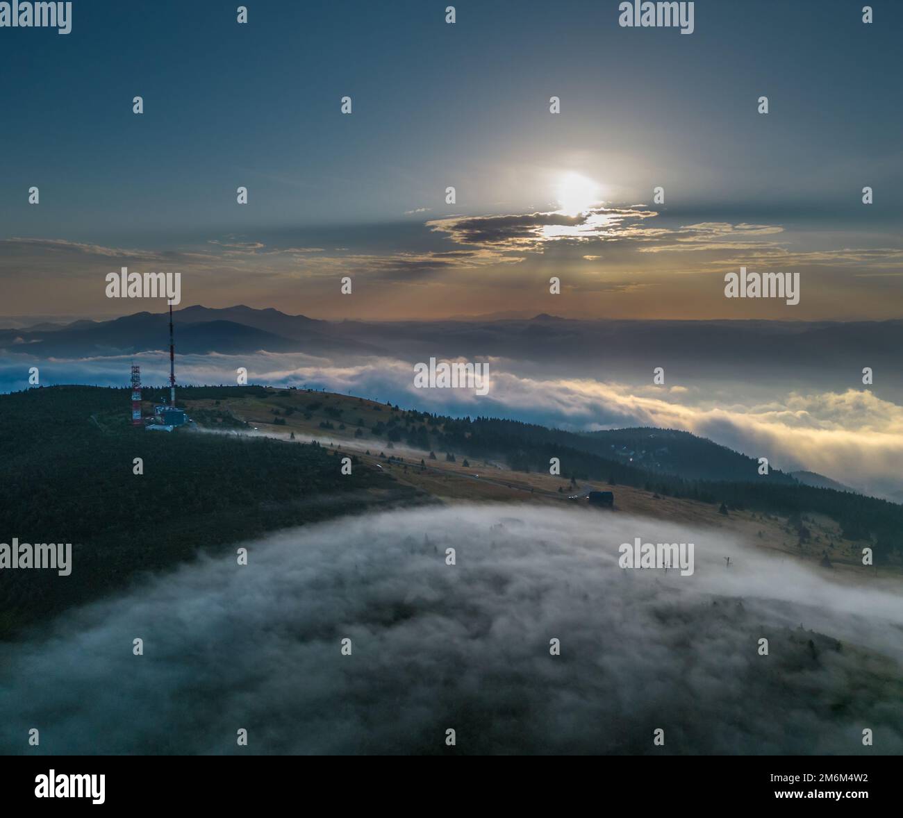 An aerial view of a tower on top of a green hill covered with clouds at ...