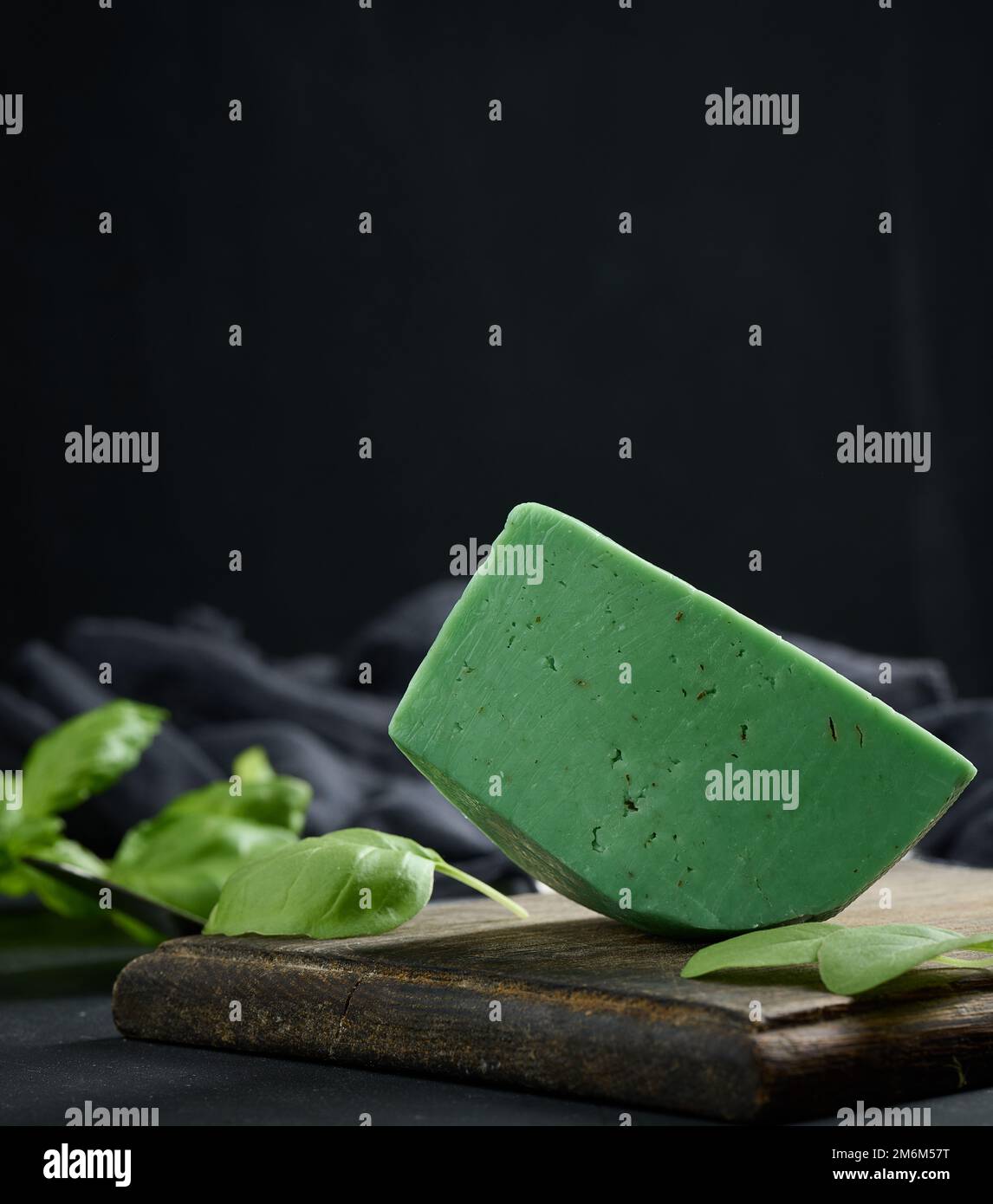 A piece of green cheese with basil on a brown wooden board, black ...