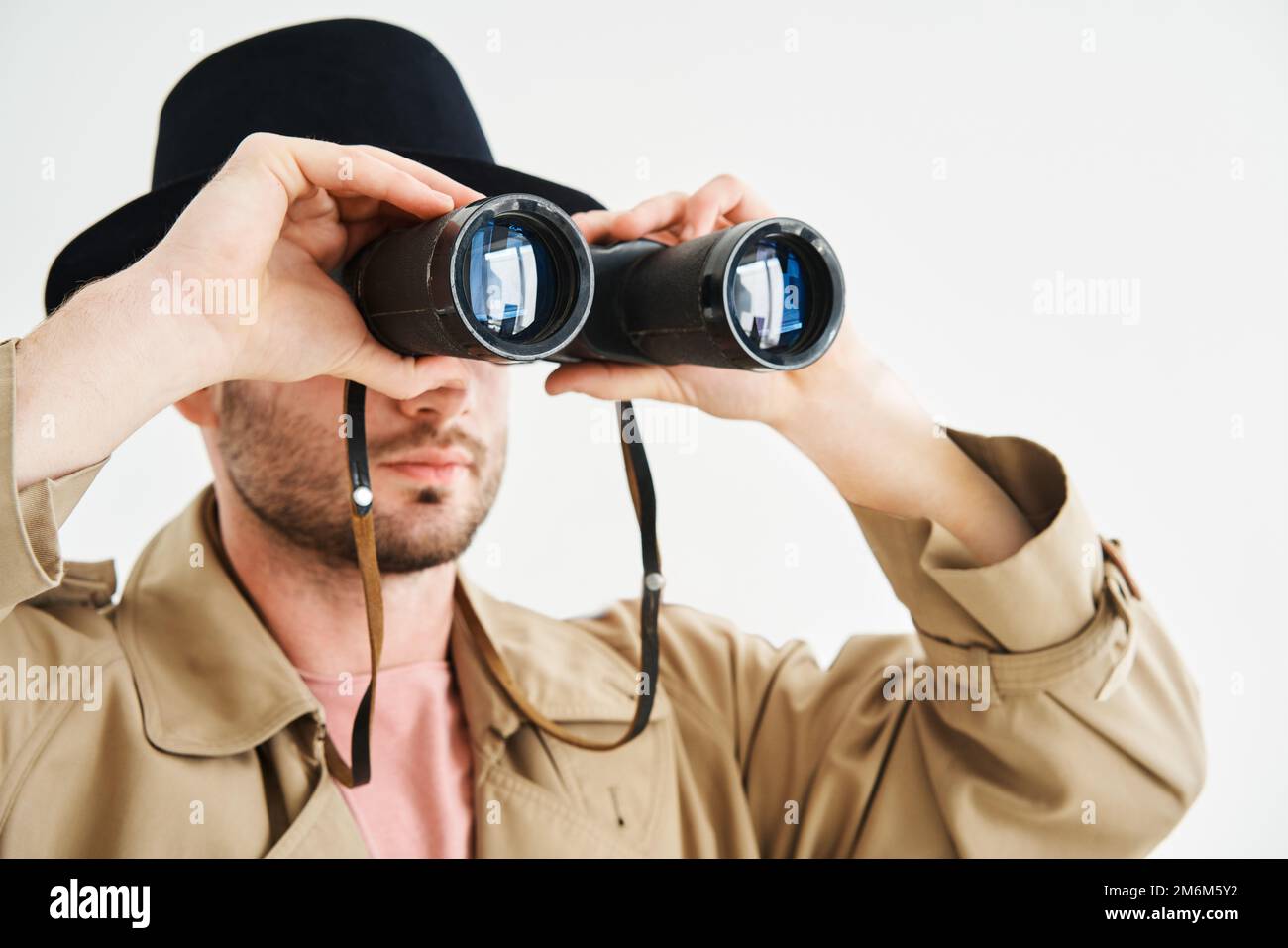 Young man wearing in coat and hat looking through binoculars over ...