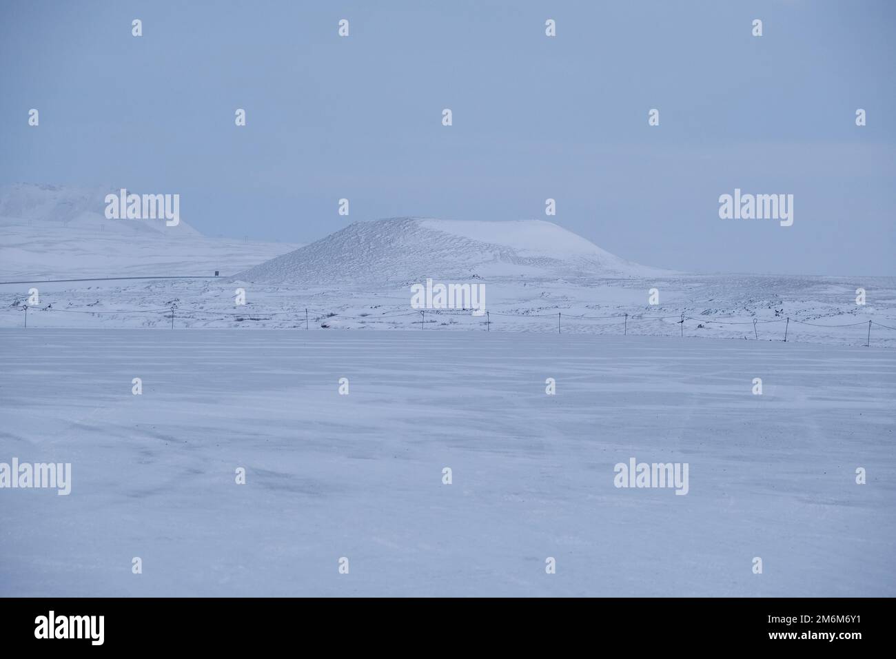 A hill in the distance and a fenced field completely covered with snow ...