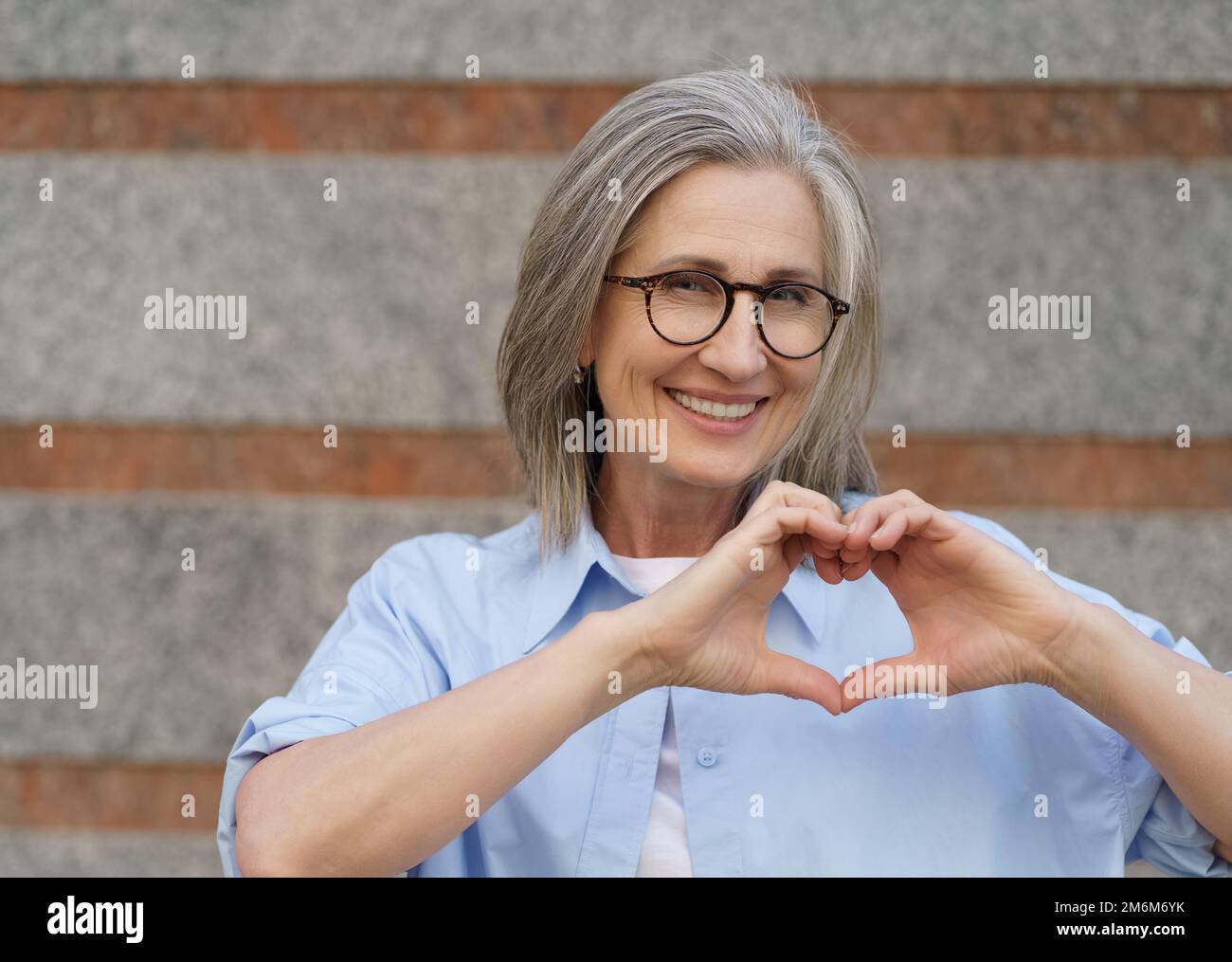 Portrait of attractive mature woman with grey hair showing heart sign ...
