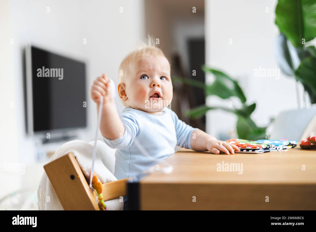 Happy infant sitting at dining table and playing with his toy in ...