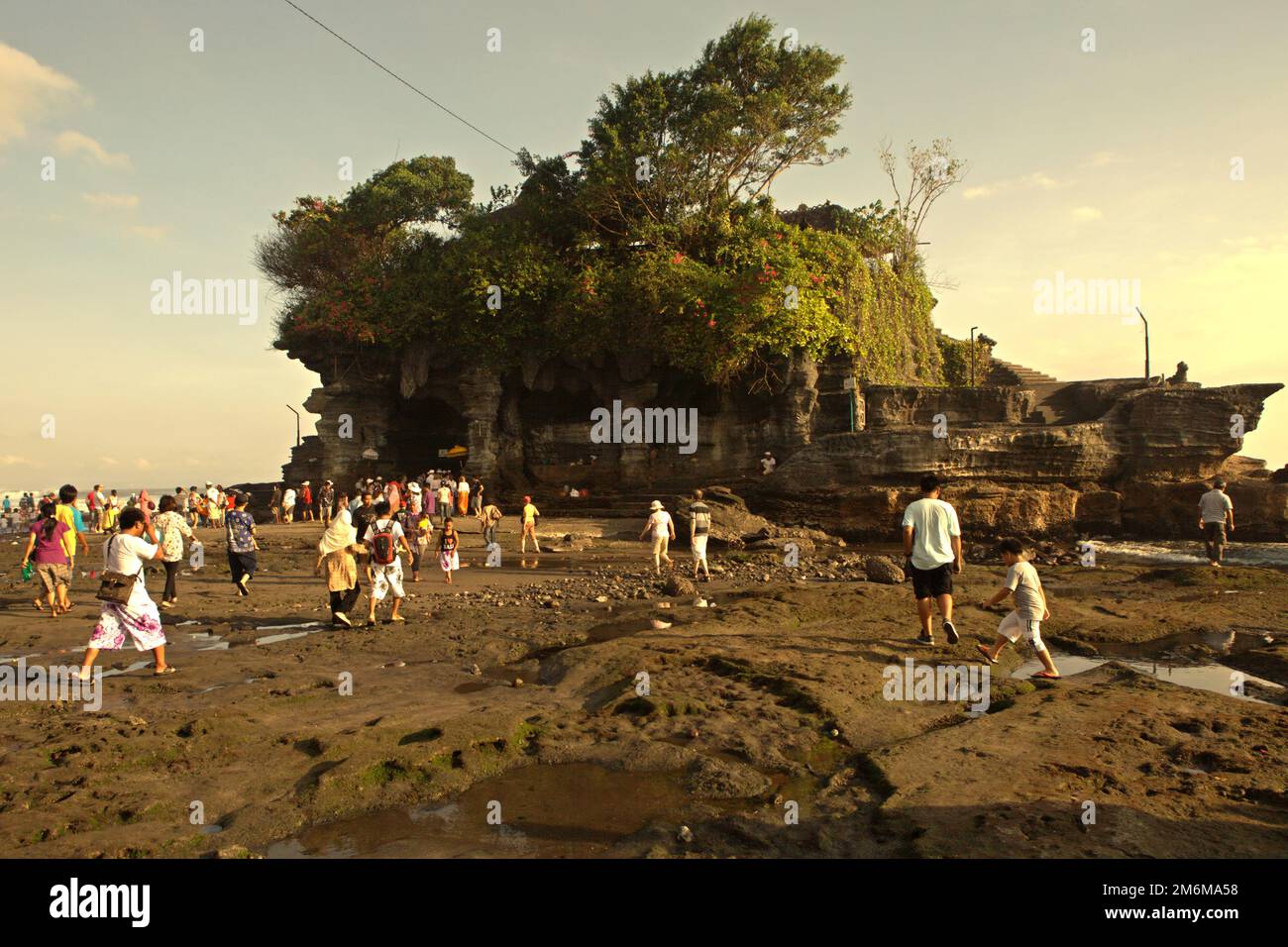 Tourists are walking on intertidal beach in a background of a hill ...