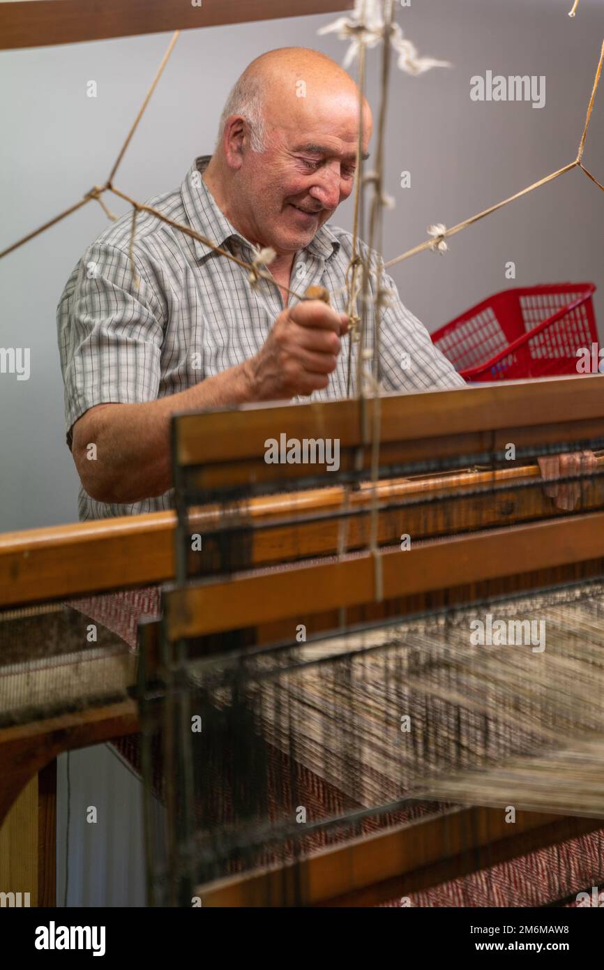 Master craftsman working on a traditional wooden loom and hand weaving ...