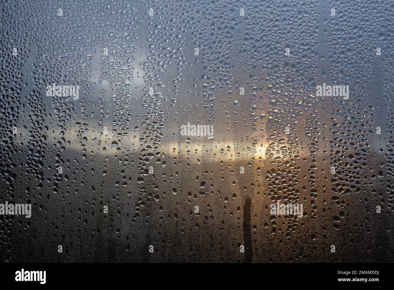 Condensation on window with a stormy sunrise outside, waterdrops on the ...