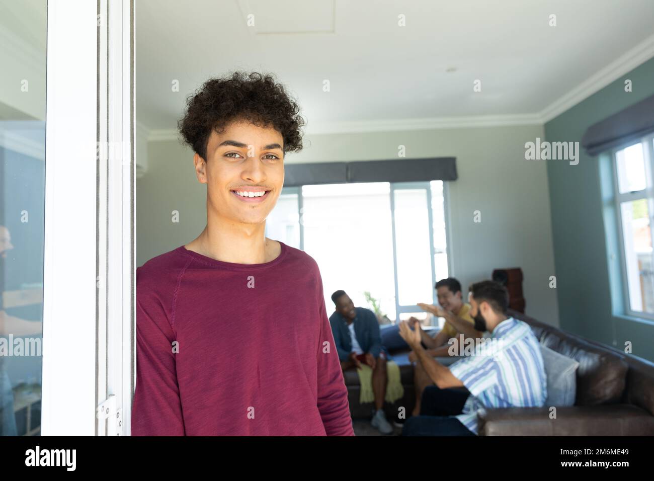 Portrait of smiling multiracial young man standing by window with ...