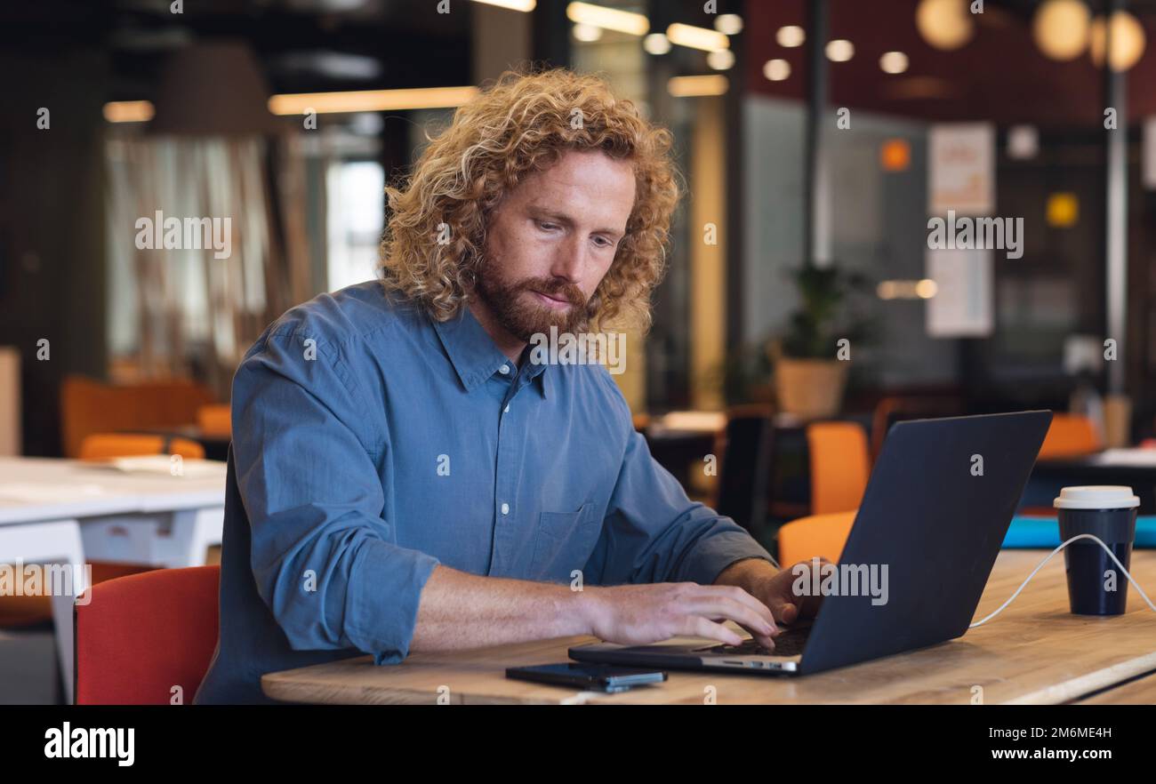 Young caucasian businessman using laptop at desk in creative office ...