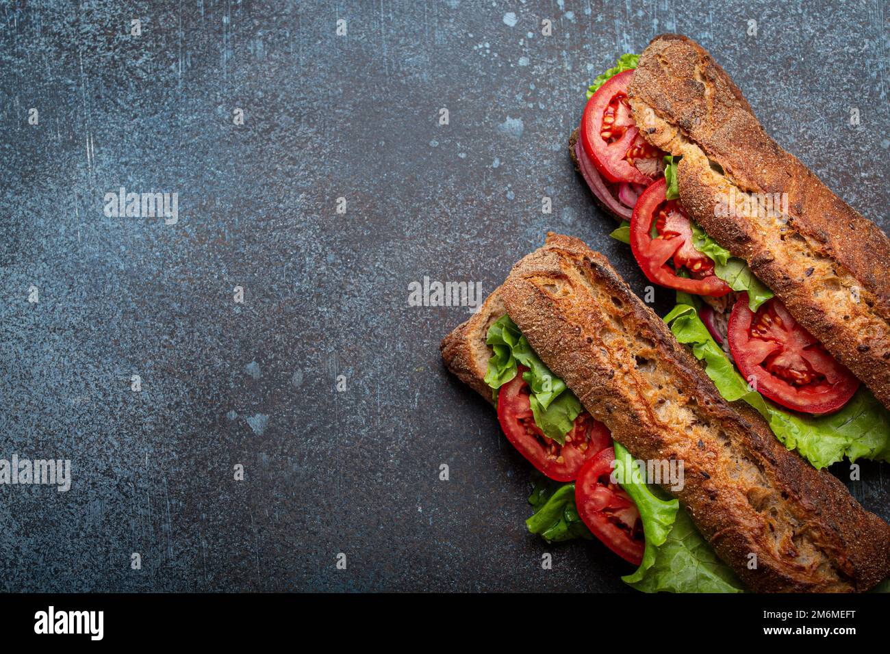 Two dark ciabatta sandwiches with green salad, ripe red tomatoes, onion ...