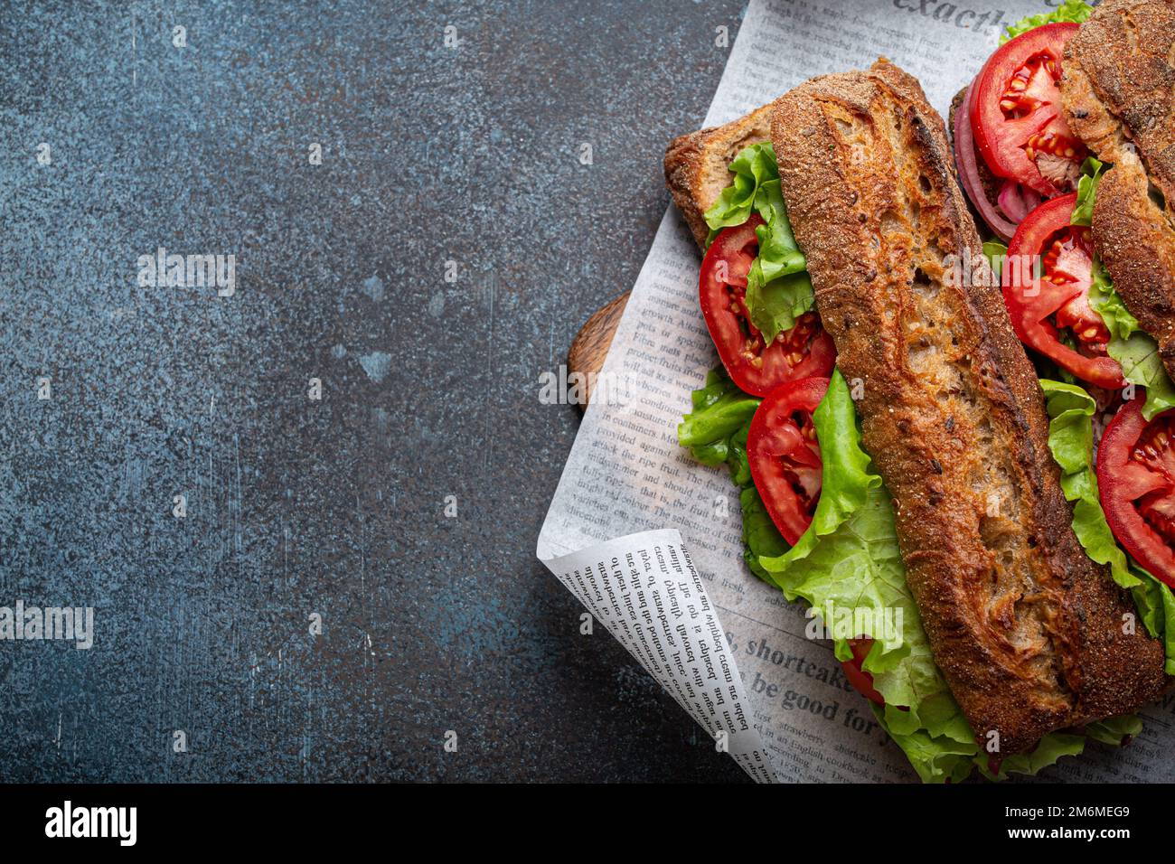 Two dark ciabatta sandwiches with green salad, ripe red tomatoes, onion ...