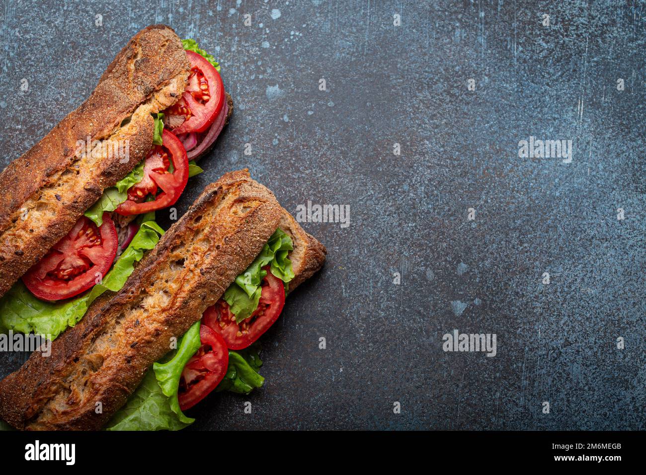 Two dark ciabatta sandwiches with green salad, ripe red tomatoes, onion ...