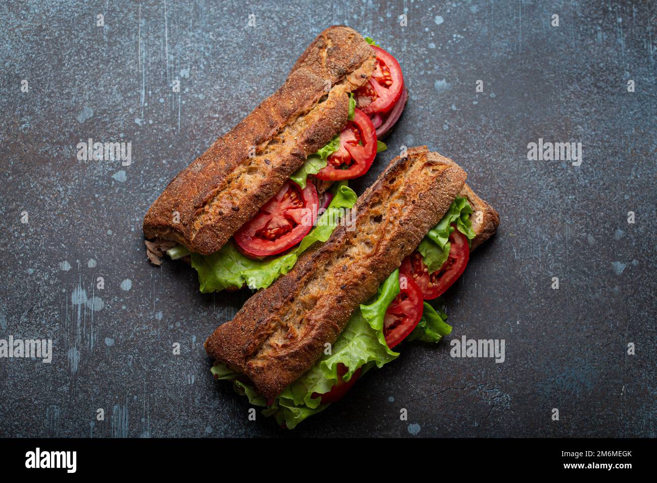 Two dark ciabatta sandwiches with green salad, ripe red tomatoes, onion ...