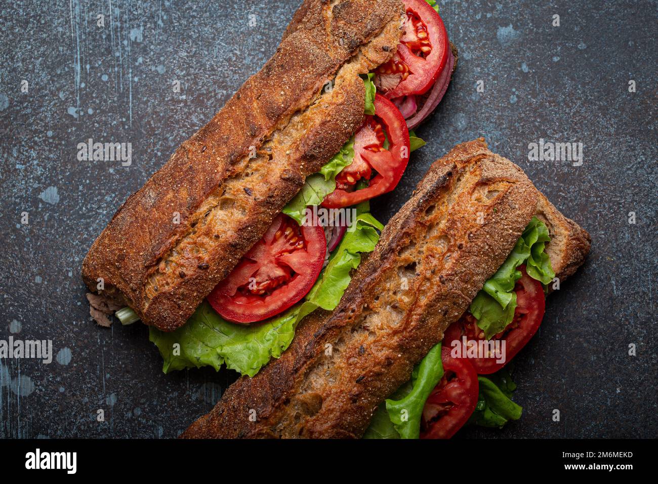 Two dark ciabatta sandwiches with green salad, ripe red tomatoes, onion ...