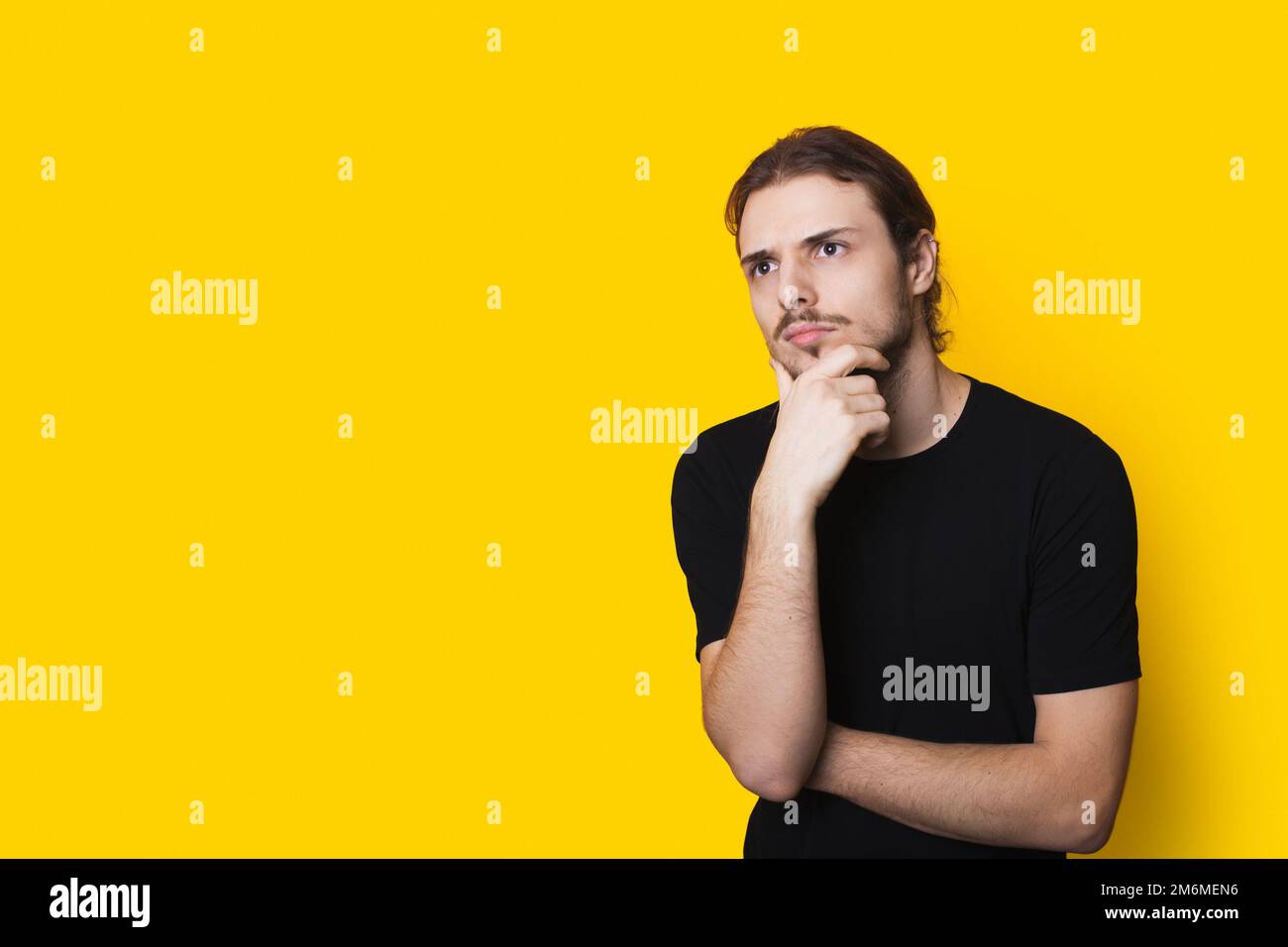 Handsome Caucasian man thinking with hand touching chin isolated over yellow studio background ...