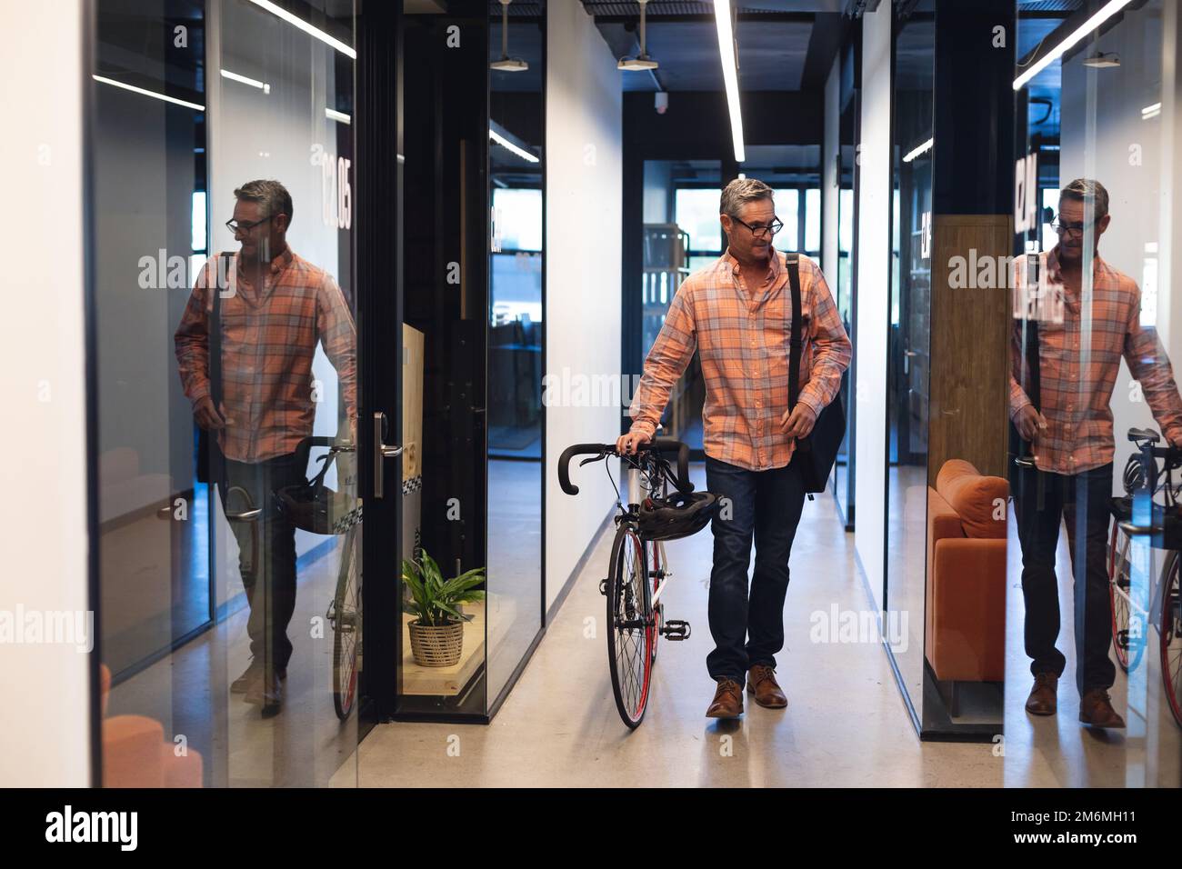 Caucasian mature businessman walking with bicycle in corridor of ...