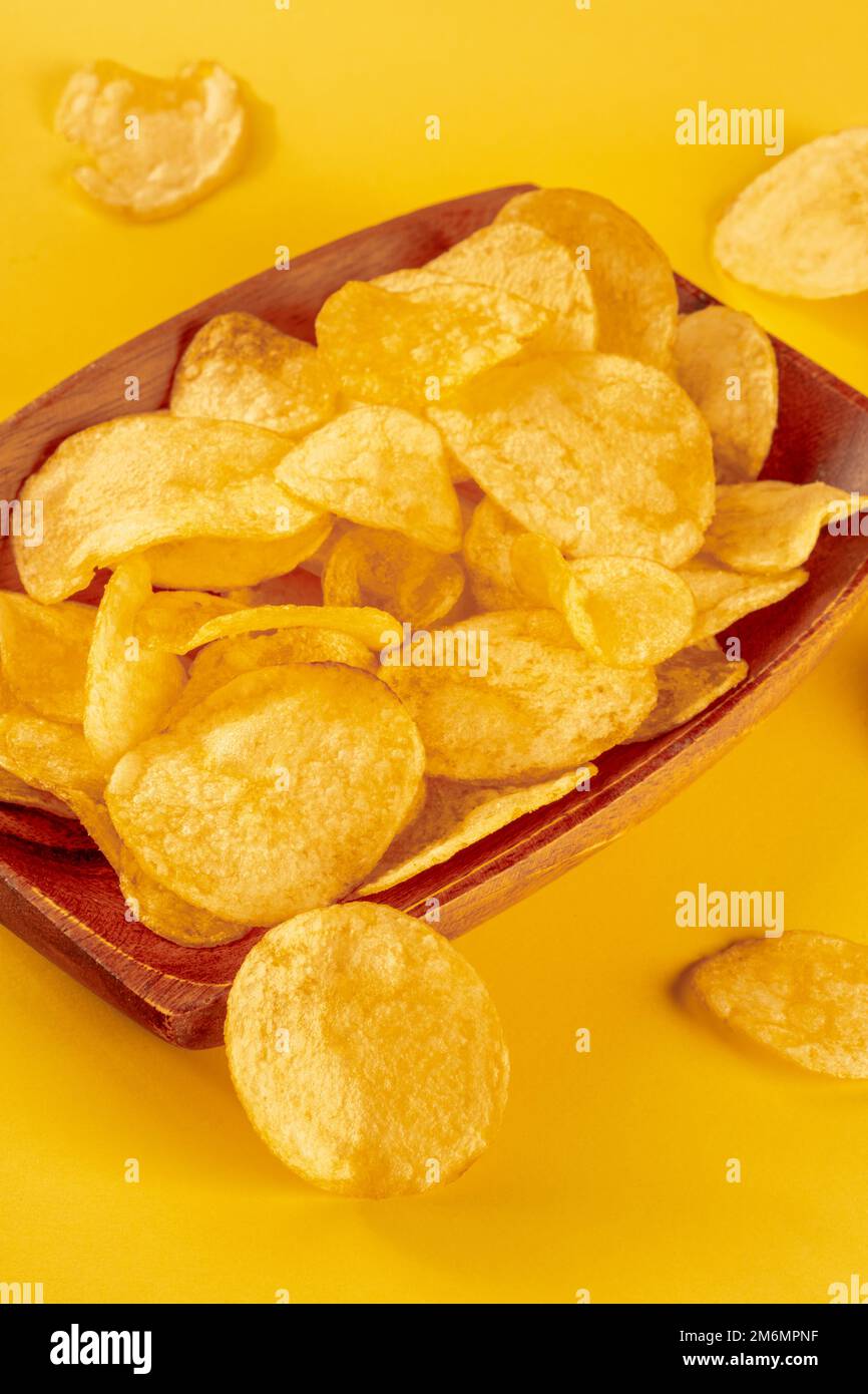 Potato chips or crisps in a bowl and scattered on a yellow background ...