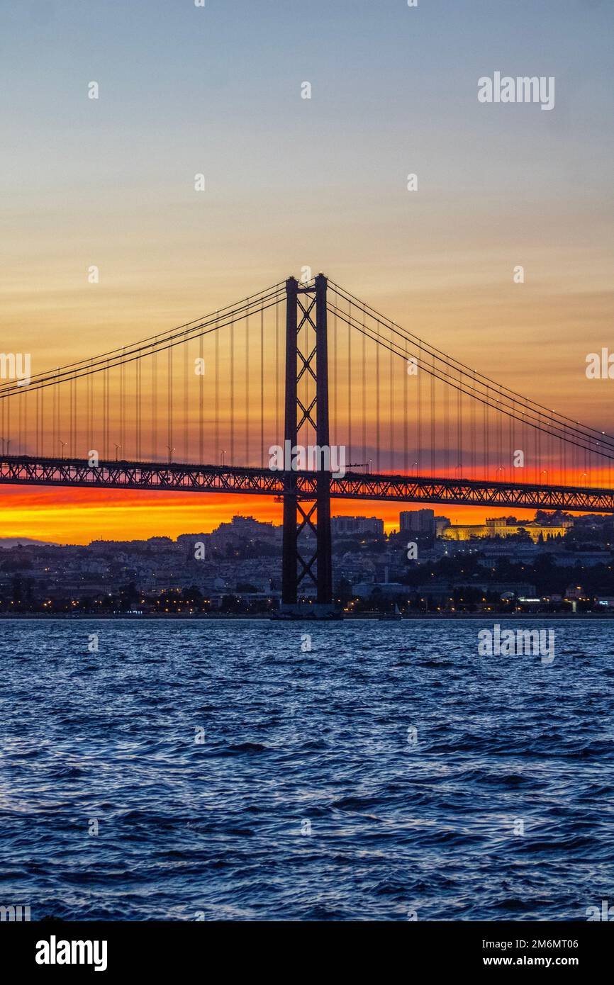 A vertical shot of the The 25 de Abril Bridge at sunset in Lisbon ...