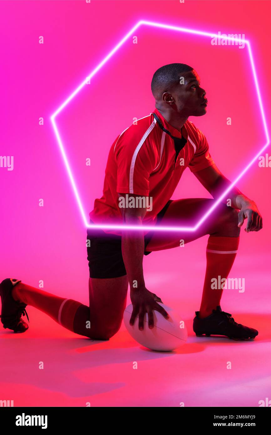 African american male player with rugby ball kneeling by illuminated ...