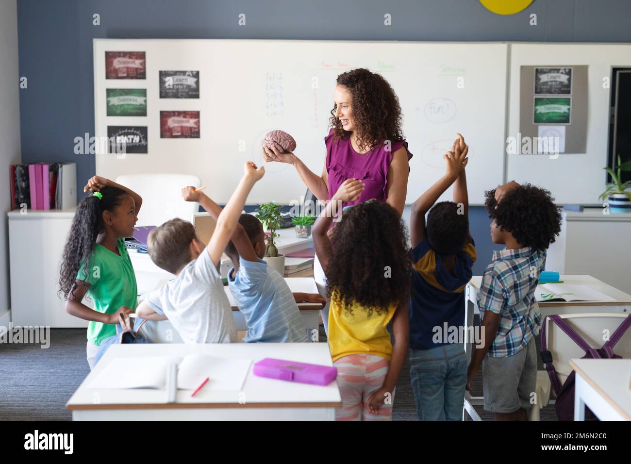 Multiracial elementary students raising hands during caucasian young ...