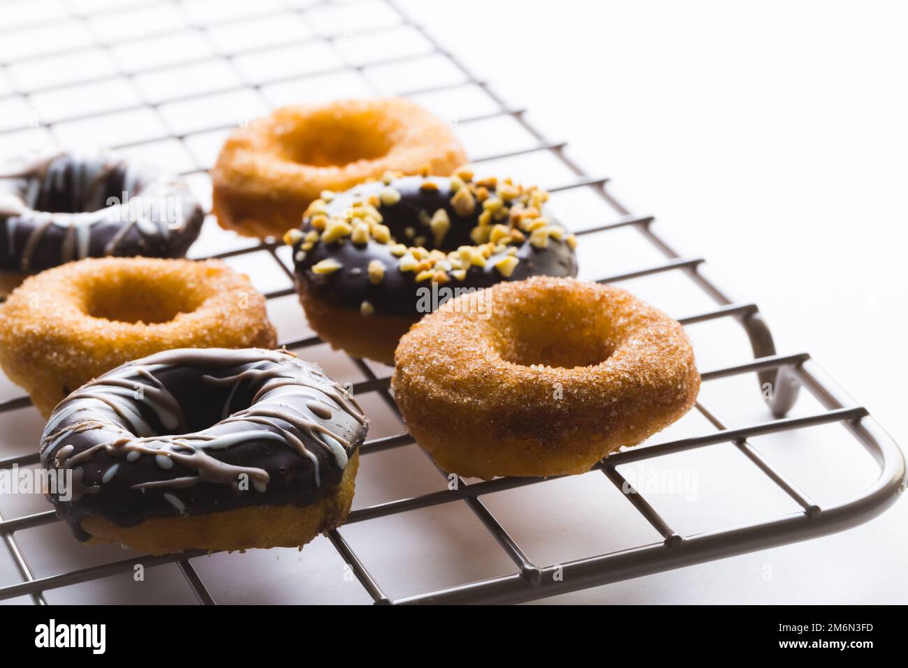 Close-up of fresh various donuts on cooling rack against white ...