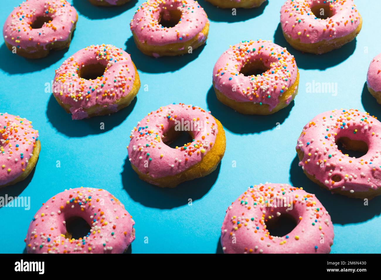 High angle view of fresh pink donuts with sprinklers arranged against ...