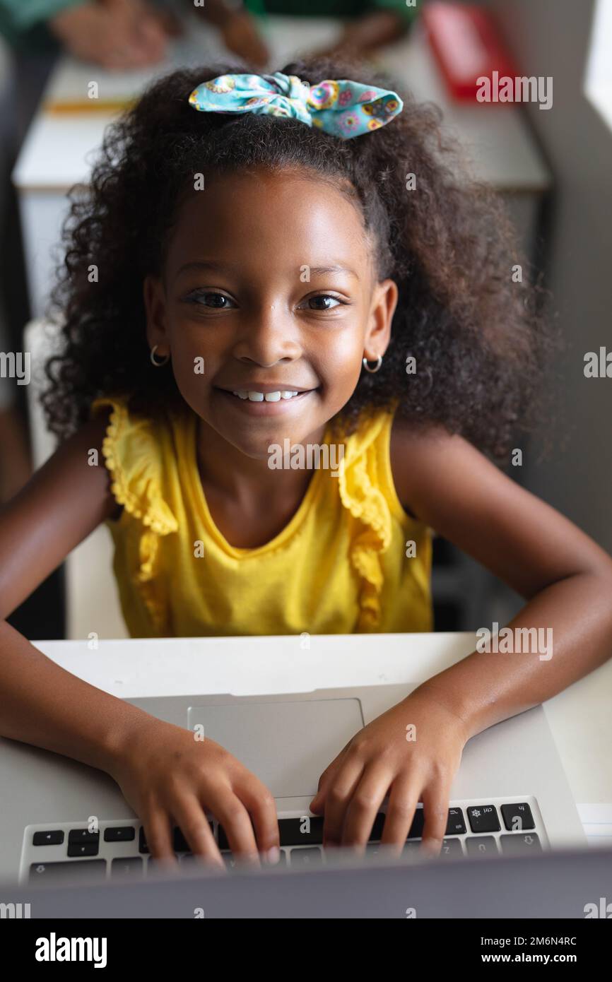 Portrait of smiling african american elementary schoolgirl using laptop ...