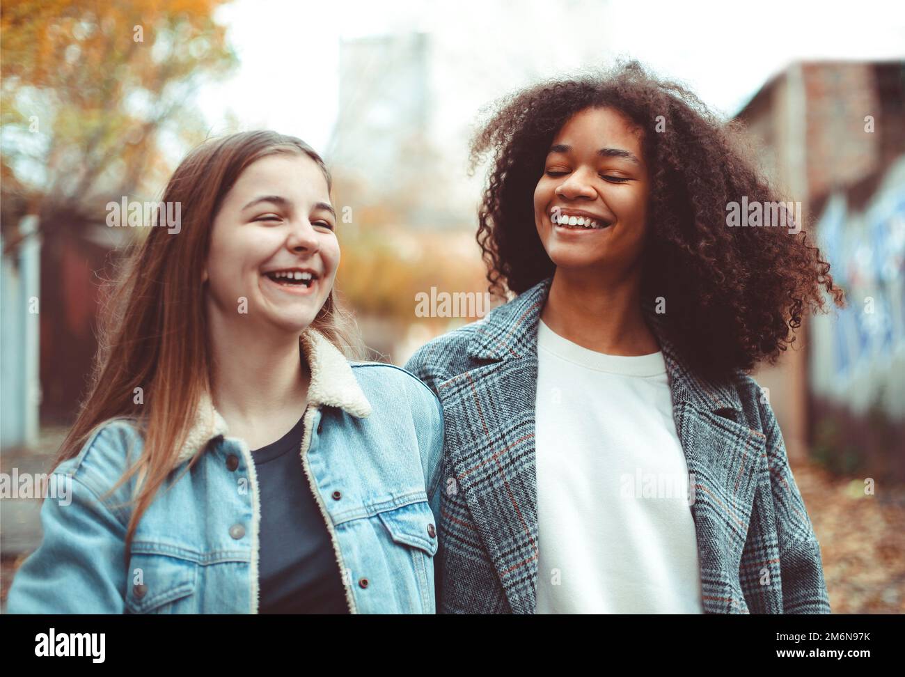 Two happy carefree multiracial girlfriends walking city street, talking ...