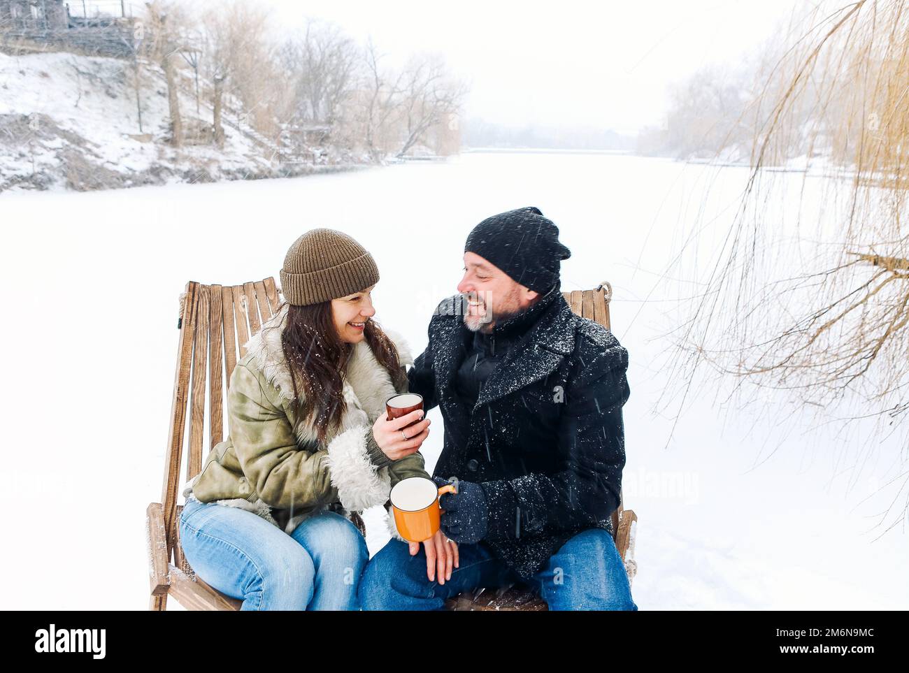 Happy lovely middle-aged couple dating on frozen lake, drinking hot tea ...