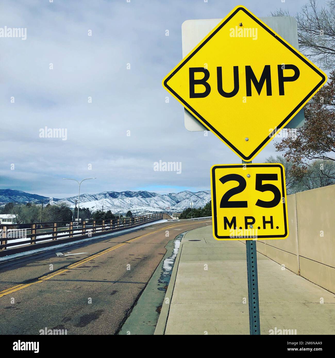 A close-up shot of bump sign with 25 M.P.H with mountains road and rail ...