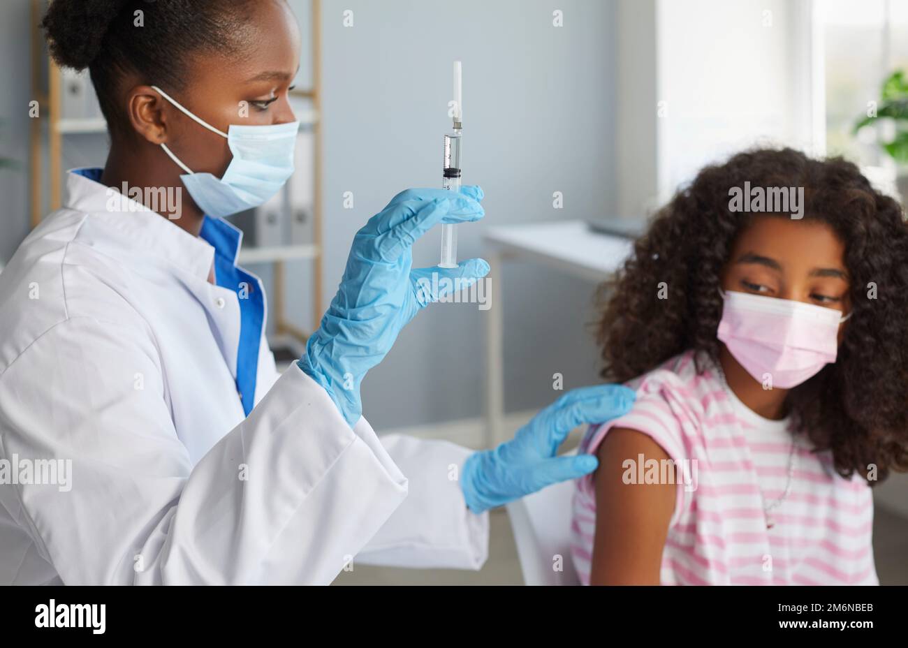 Doctor is giving a vaccine injection to teen girl in shoulder in clinic ...