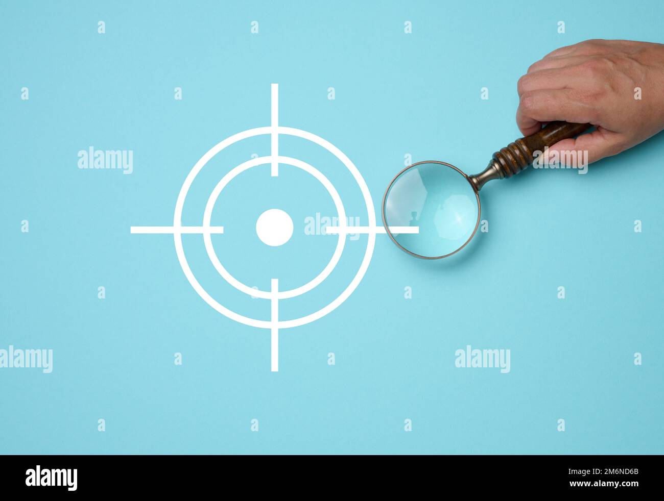 Female hand holding wooden magnifier and target icon on blue background ...