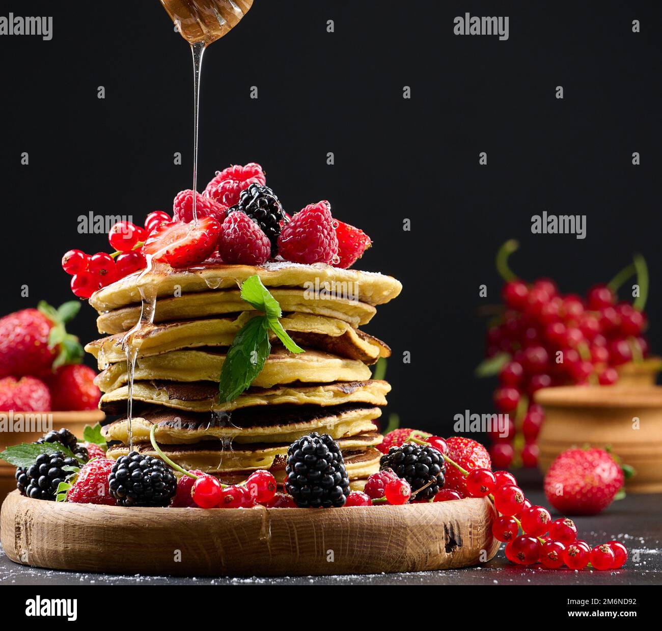 Stack of pancakes with fresh fruit sprinkled with honey on a black ...