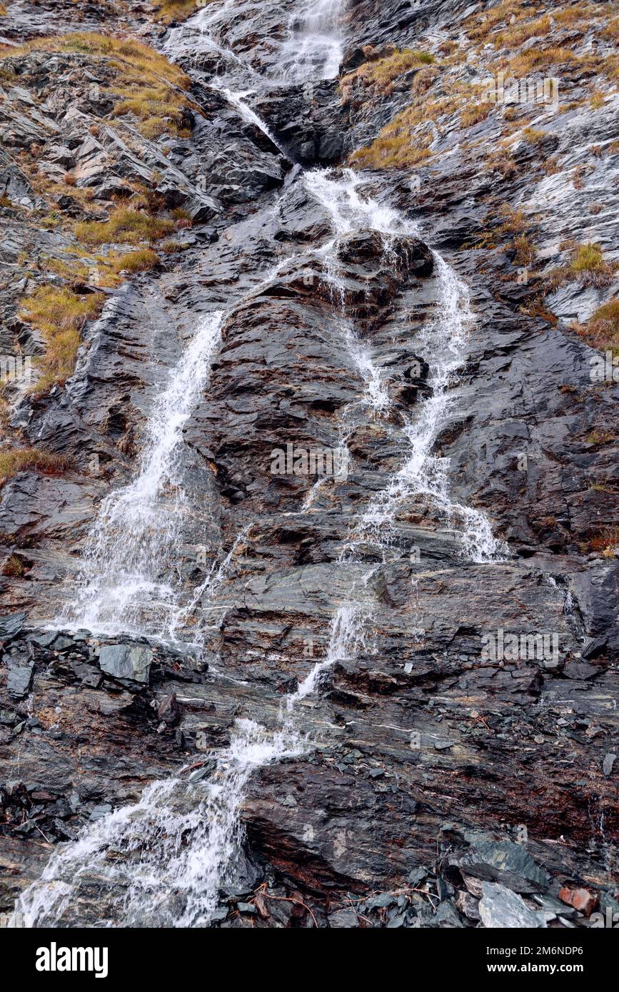 Small mountain waterfall flows over granite ledges of alpine rocks ...