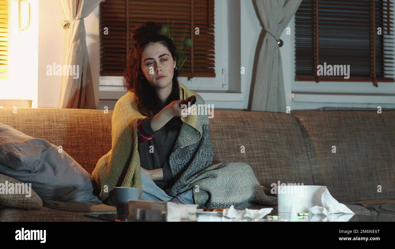 Flu and headache. Sad young Caucasian woman sitting on sofa covered ...