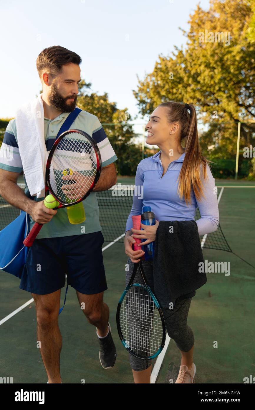 Happy caucasian couple holding rackets and water bottles talking on ...
