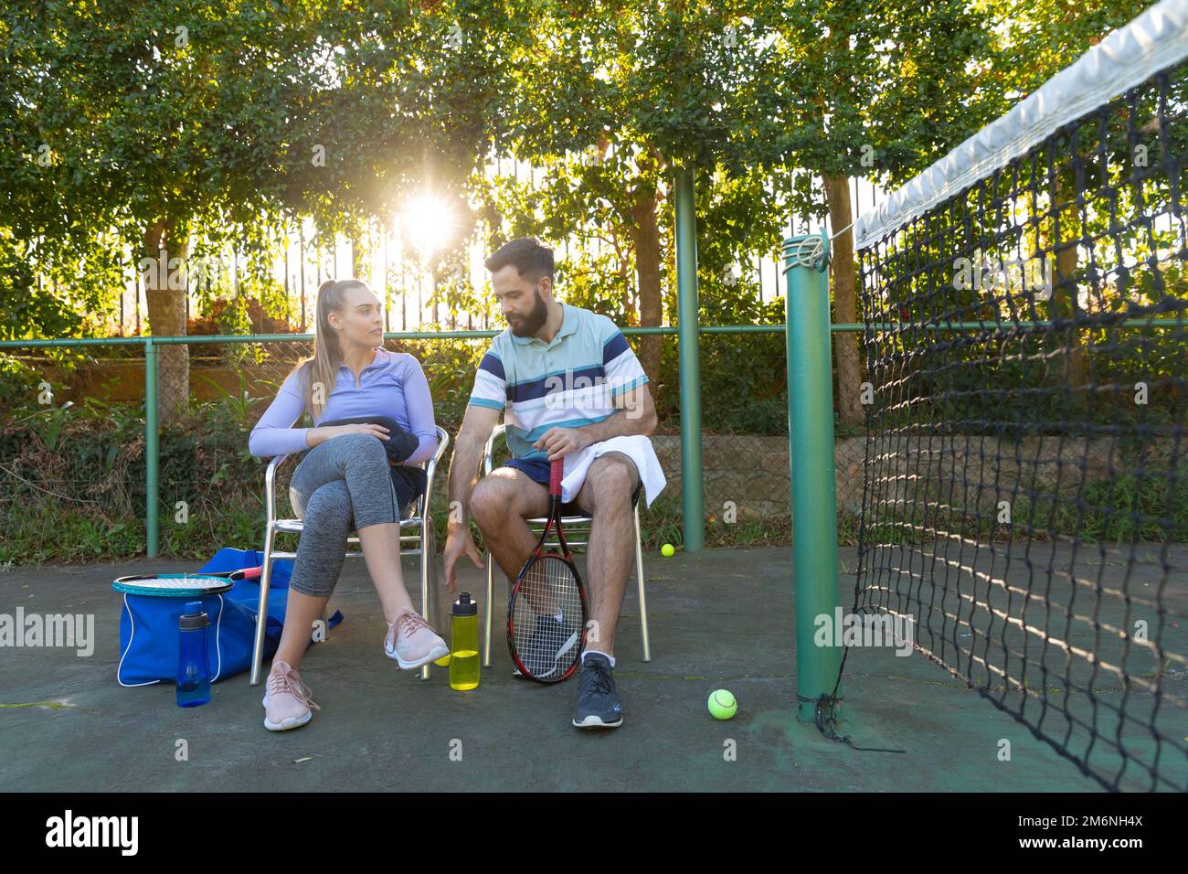 Caucasian couple playing tennis sitting on chairs talking at the side ...