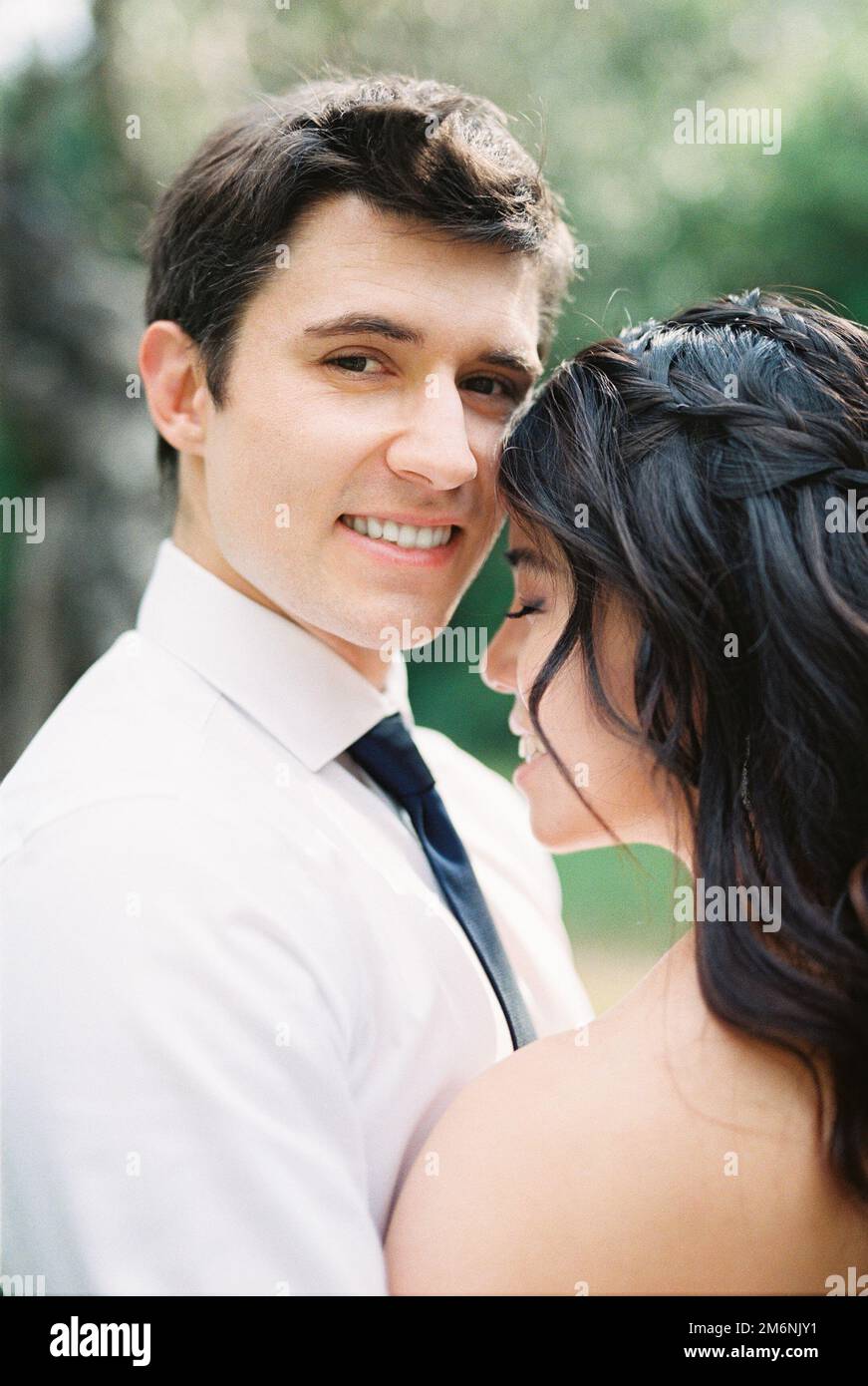 Bride touches her forehead to the cheek of the smiling groom. Portrait ...