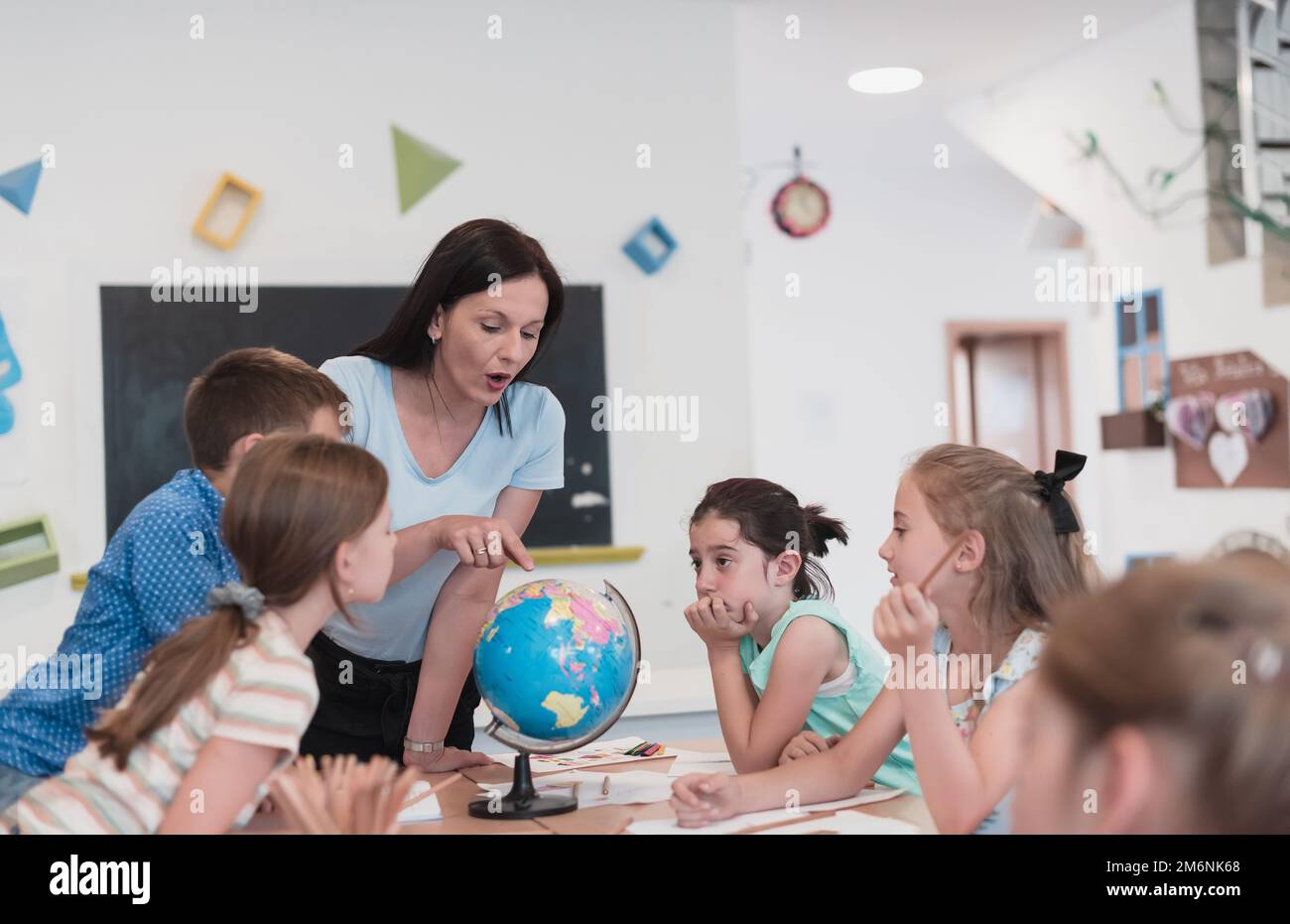 Female teacher with kids in geography class looking at globe. Side view ...