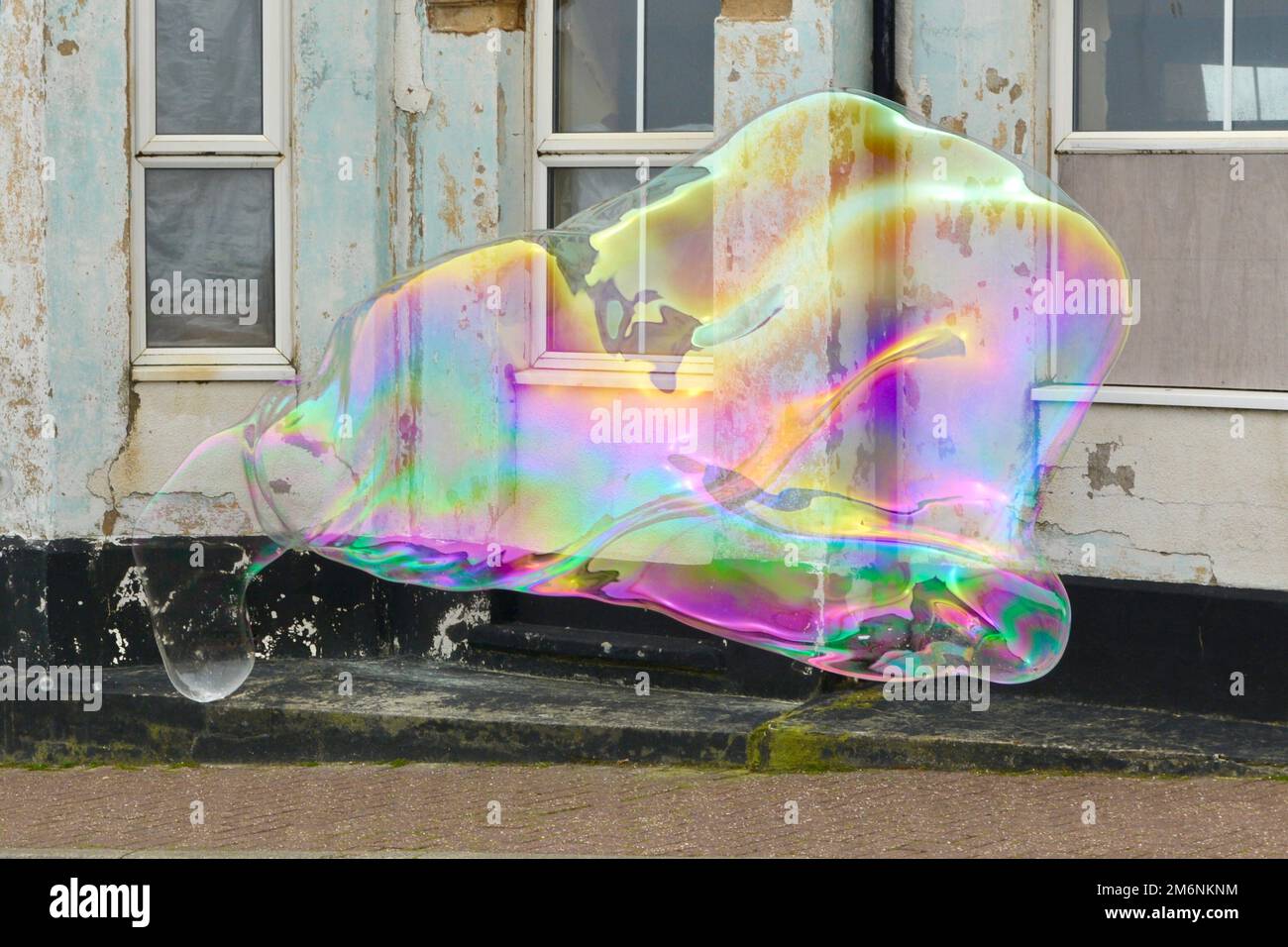 Rainbow coloured giant soap bubble floating past a derelict building ...
