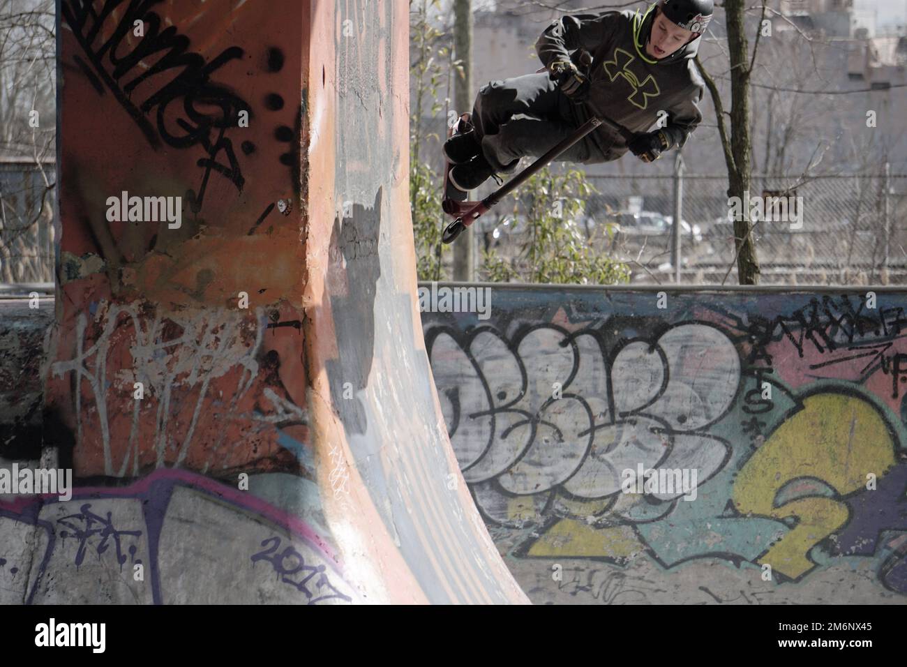 A boy doing kick scooter tricks in the skate park with graffiti on the ...