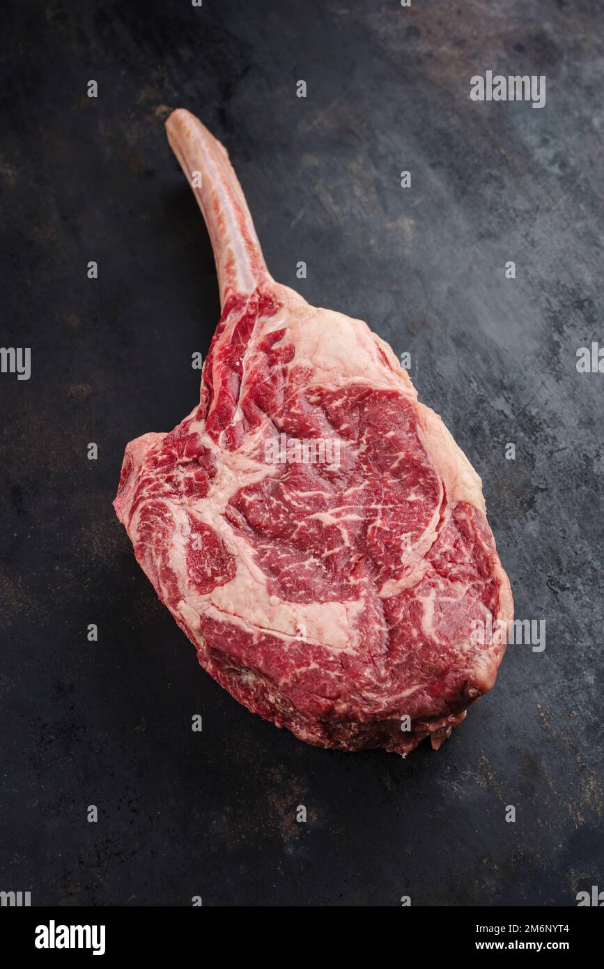 Raw dry aged wagyu tomahawk steak offered as close-up on an old black ...