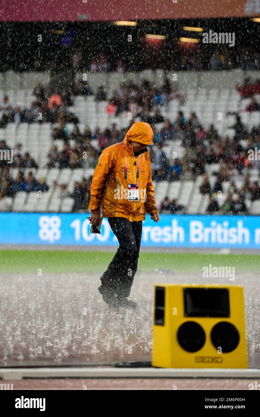 An official walking across the track and field in pouring rain at the ...