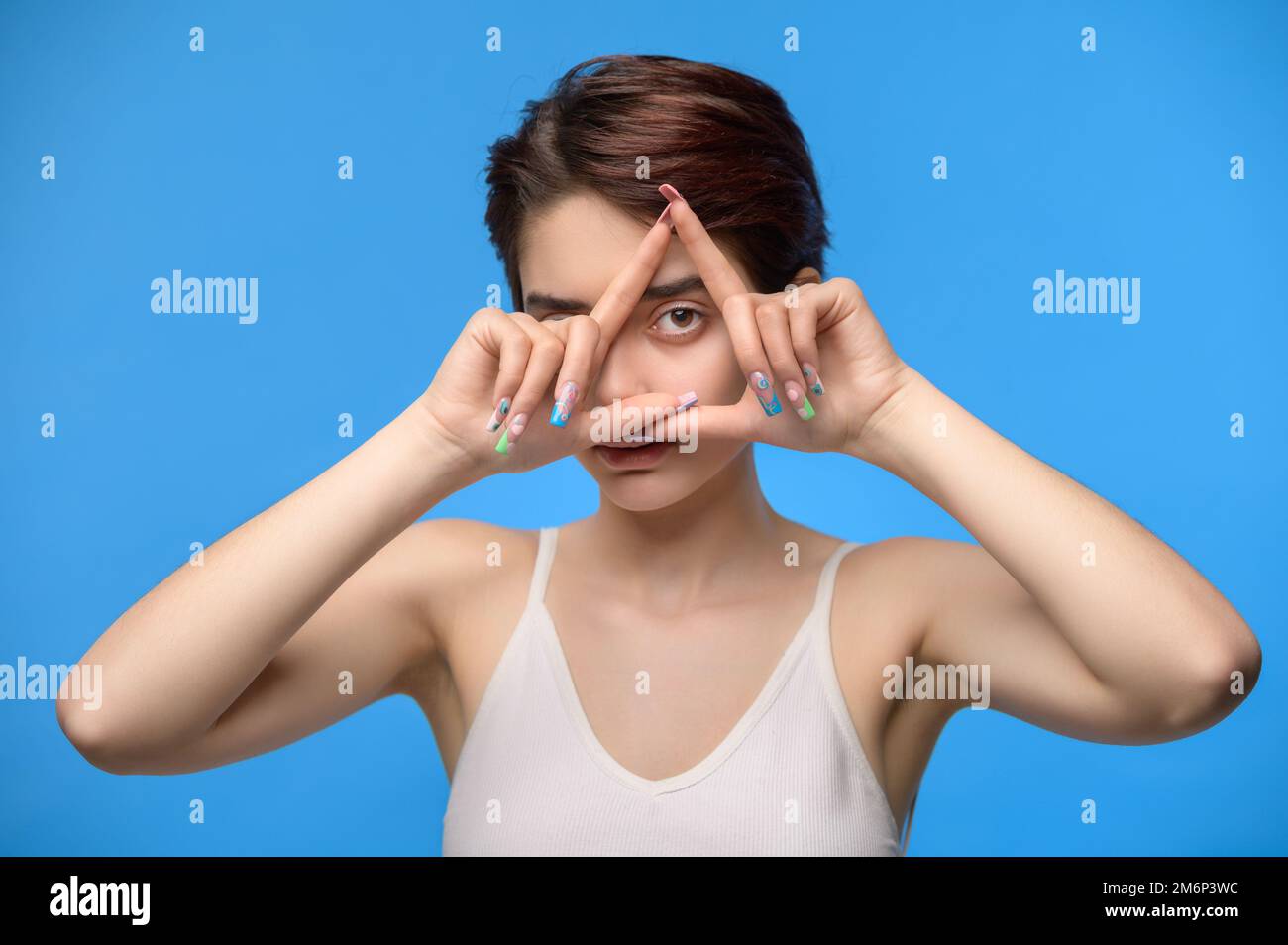 Young brunette woman looking through triangle finger frame Stock Photo ...
