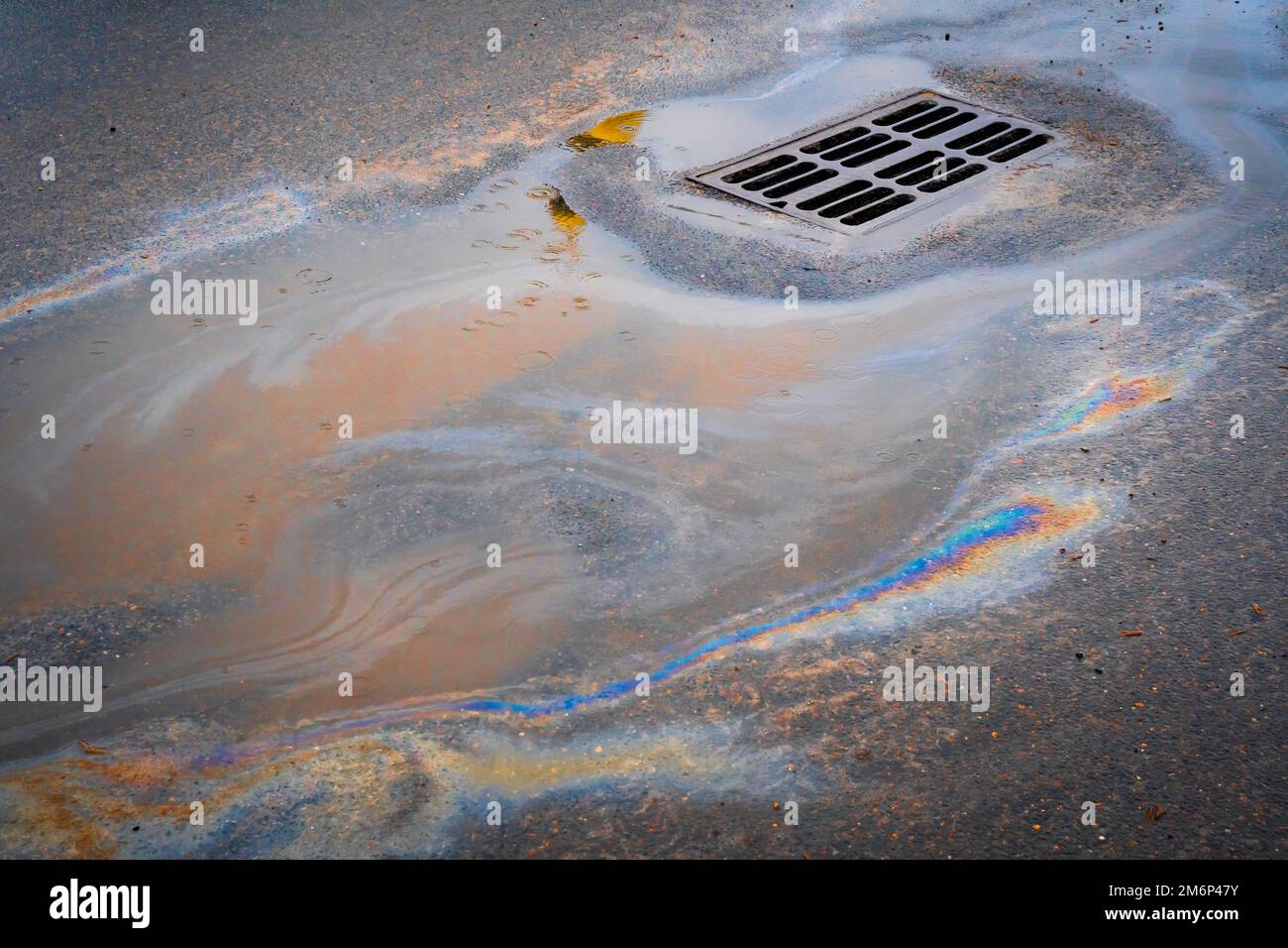 Oil slick on the asphalt road background drains into the storm drain ...