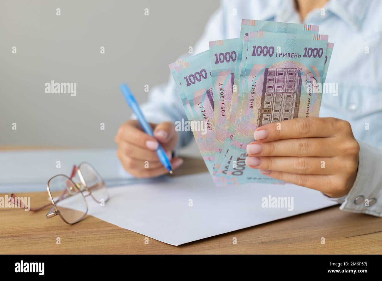 Woman holding Ukrainian 1000 bill banknotes and making notes on a blank ...